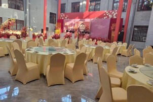 Uma sala de banquetes com mesas redondas e cadeiras, um palco com decorações florais e um fundo vermelho.