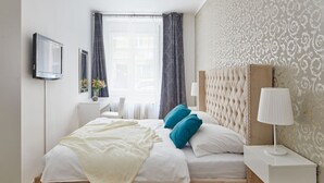 Quarto de hotel com cama, mesa de cabeceira com abajur, televisão na parede e janela com cortinas.
