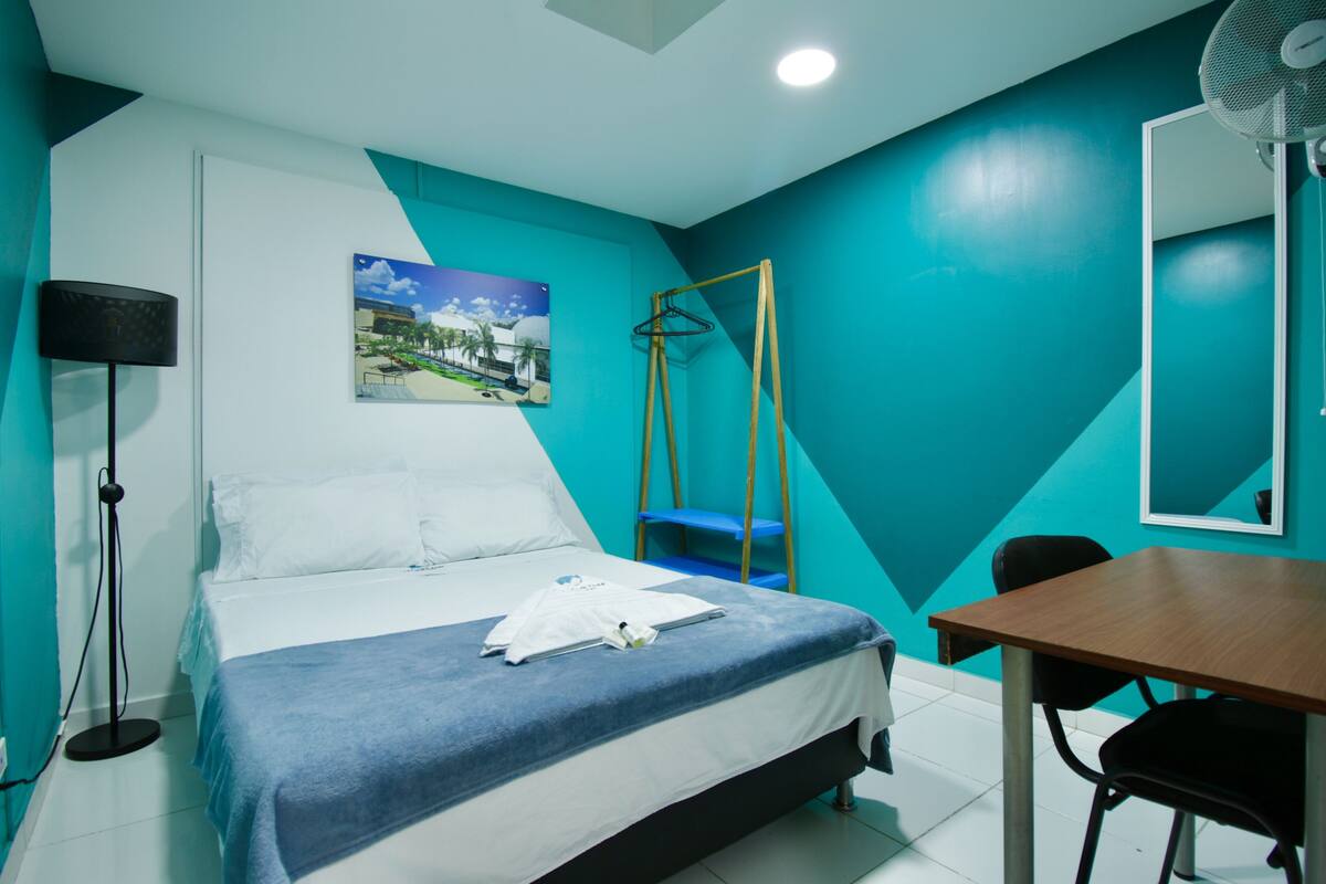 Quarto de hotel com cama, escrivaninha, cadeira, cadeira suspensa, luminária, pintura e espelho.
