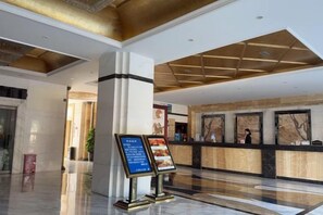 Um hall de hotel com uma mesa de recepção, um pilar grande e uma placa informativa azul.