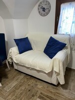 Um sofá branco com almofadas azuis numa sala com piso de madeira e um relógio de parede.