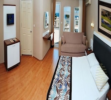 Quarto de hotel com cama, sofá, escrivaninha e vista para o mar.