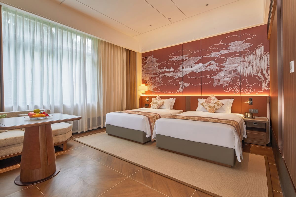 Quarto de hotel com duas camas, uma mesa de jantar e um detalhe decorativo na parede.