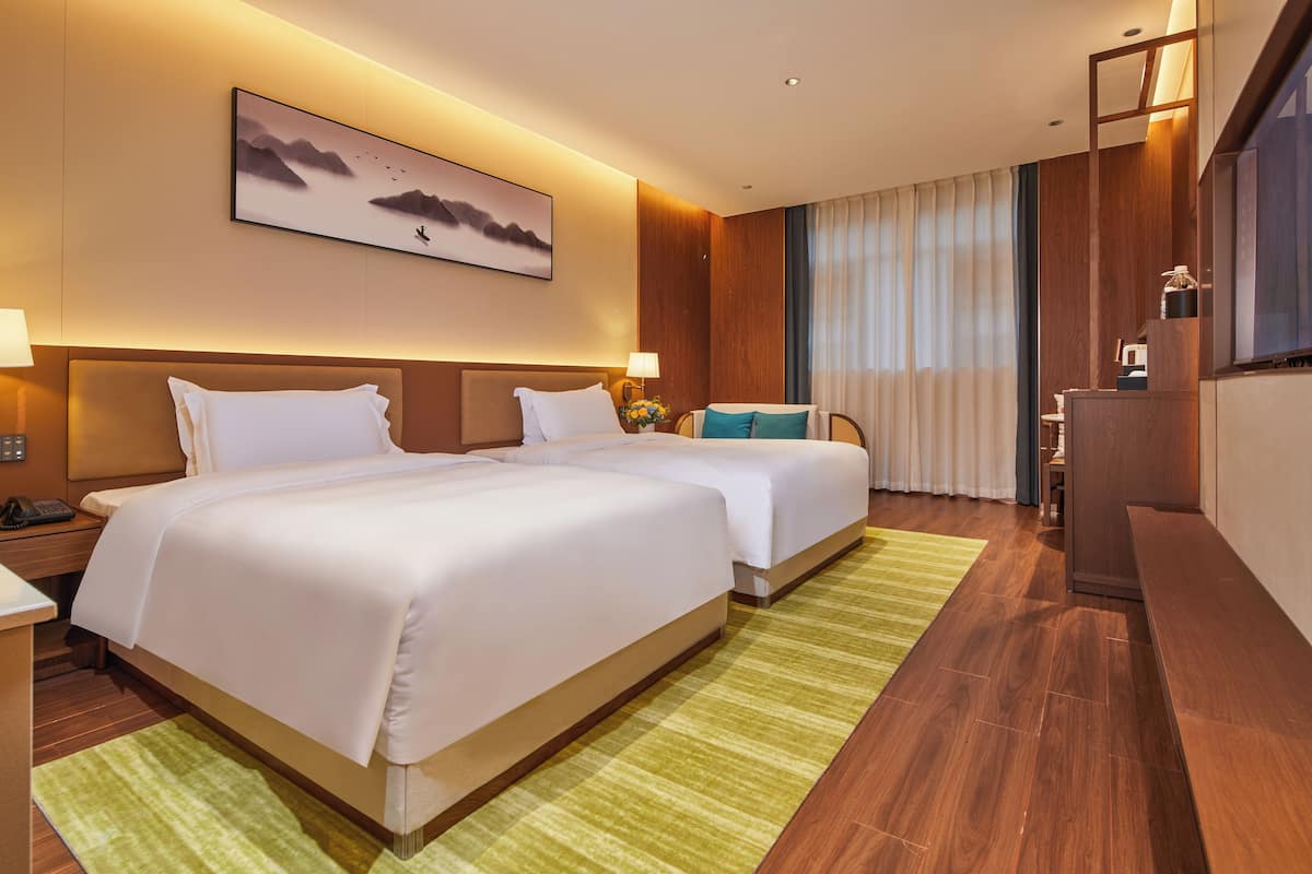 Quarto de hotel com duas camas, uma pintura grande, uma escrivaninha de madeira e uma televisão.