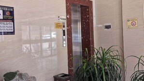 Um elevador com acabamento em mármore, cercado por paredes com diversos avisos, incluindo um sinal de proibido fumar.