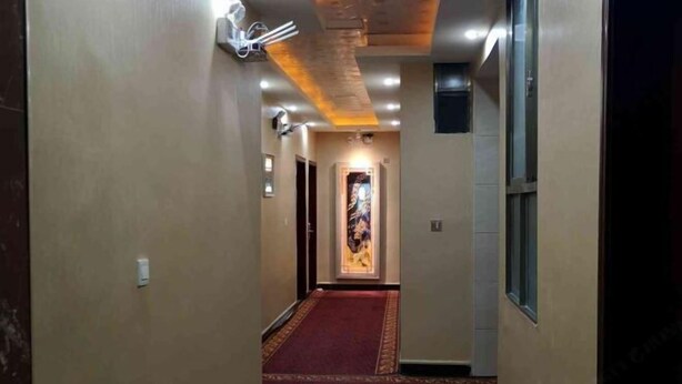 Um corredor com carpete vermelho, teto com iluminação embutida e uma porta no final.