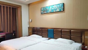 Quarto de hotel com duas camas, uma cabeceira de madeira, um quadro na parede e uma escrivaninha com uma cadeira.