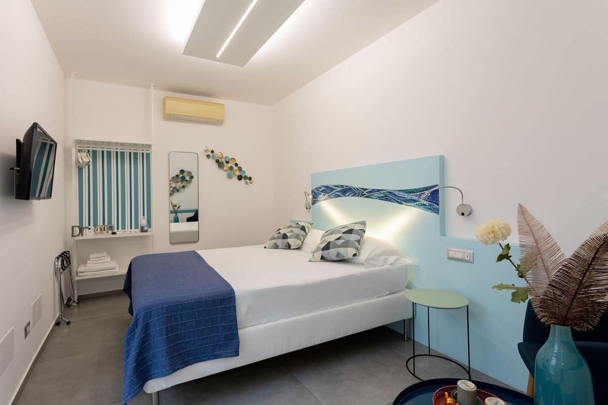 Quarto moderno com cama, mesa de cabeceira e televisão presa à parede.