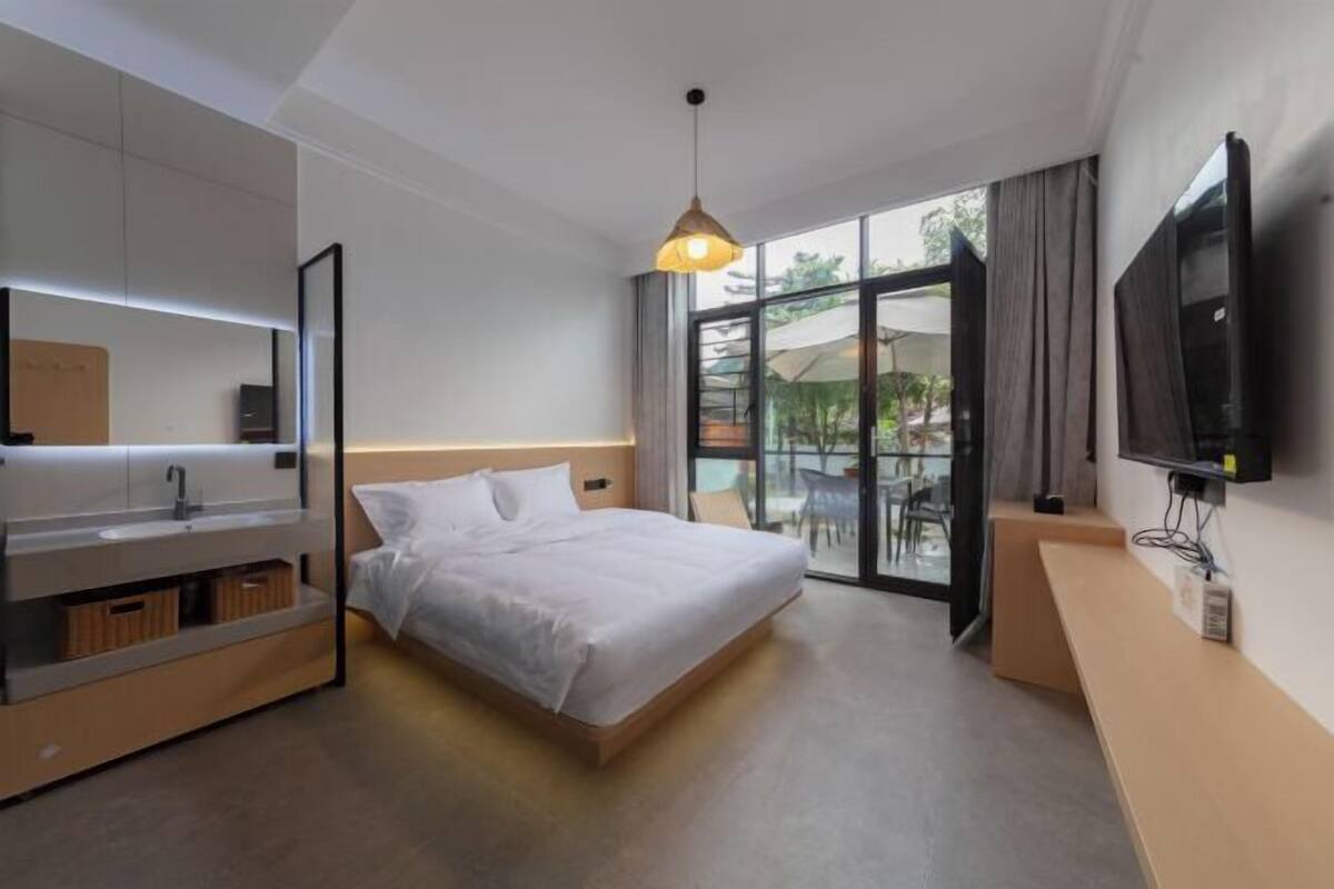 Quarto de hotel moderno com cama, televisão, janela grande e varanda.