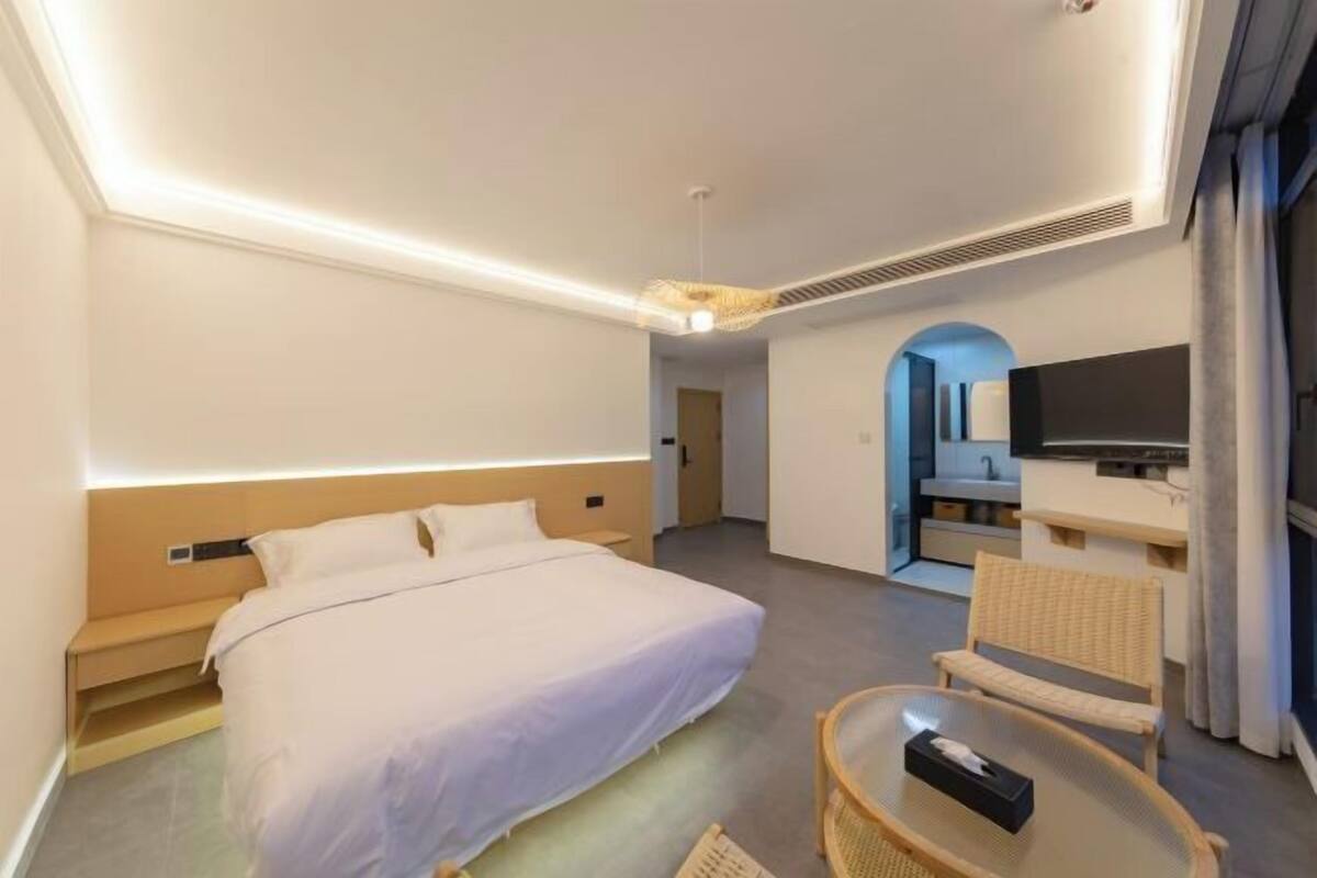 Quarto de hotel com cama, televisão, área de estar e banheiro visível por um arco.