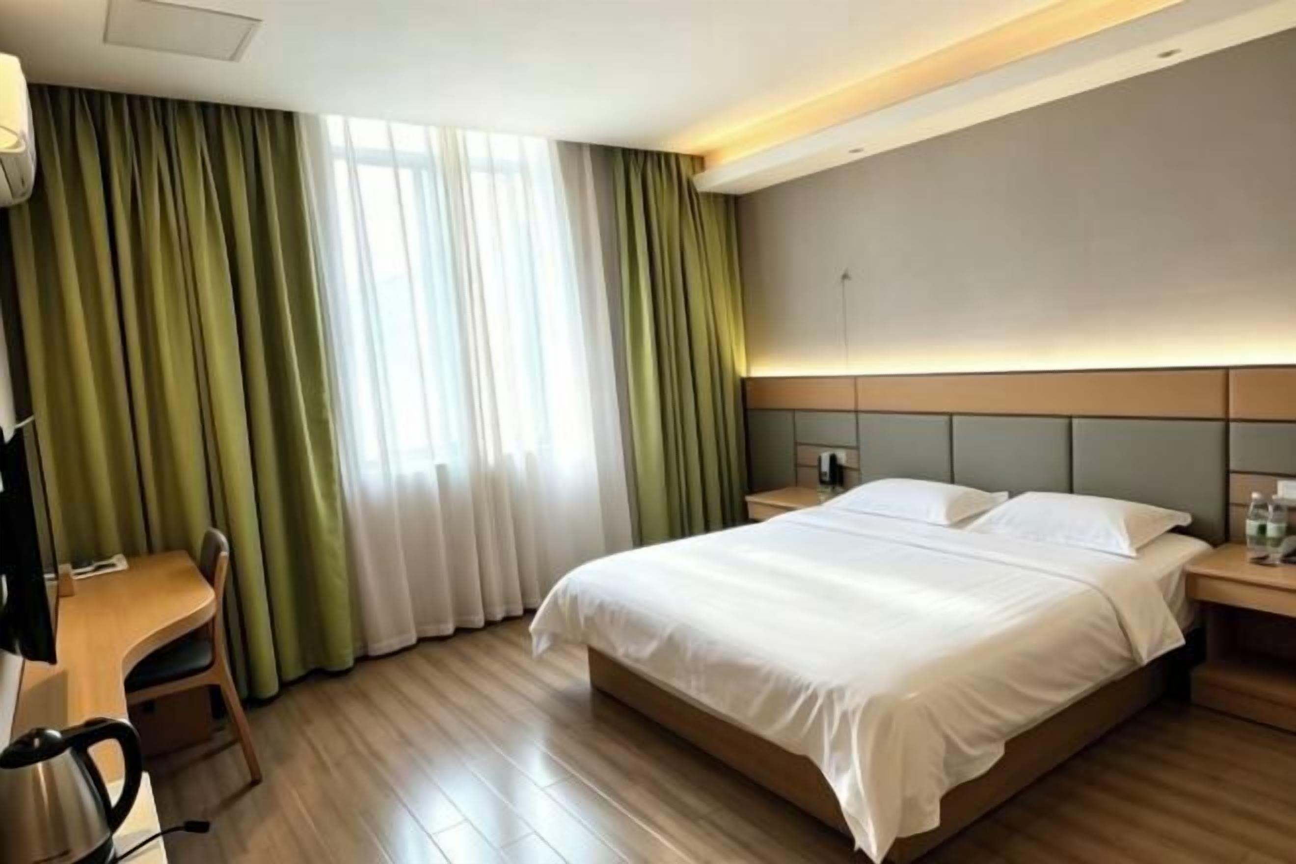 Quarto de hotel com cama, escrivaninha, cadeira, mesa de cabeceira e janela com cortinas.