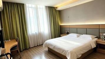 Quarto de hotel com cama, escrivaninha, cadeira, mesa de cabeceira e janela com cortinas.