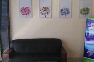 Um sofá de couro preto apoiado em uma parede com quatro obras de arte emolduradas retratando árvores em diversas cores.