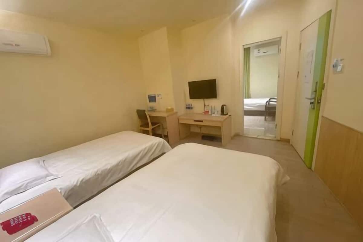 Quarto de hotel com duas camas, uma mesa com cadeira, televisão e banheiro visível por uma porta aberta.