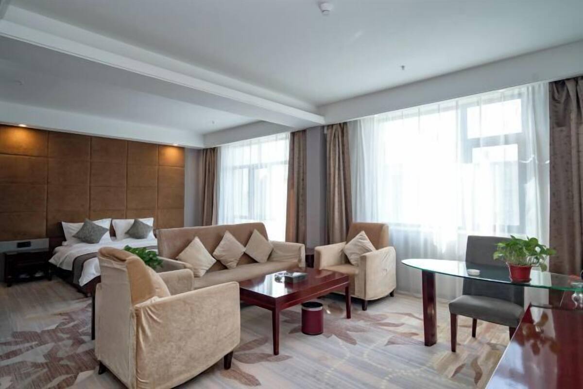 Quarto de hotel moderno com sofá, mesa de jantar de vidro e cama com cabeceira.