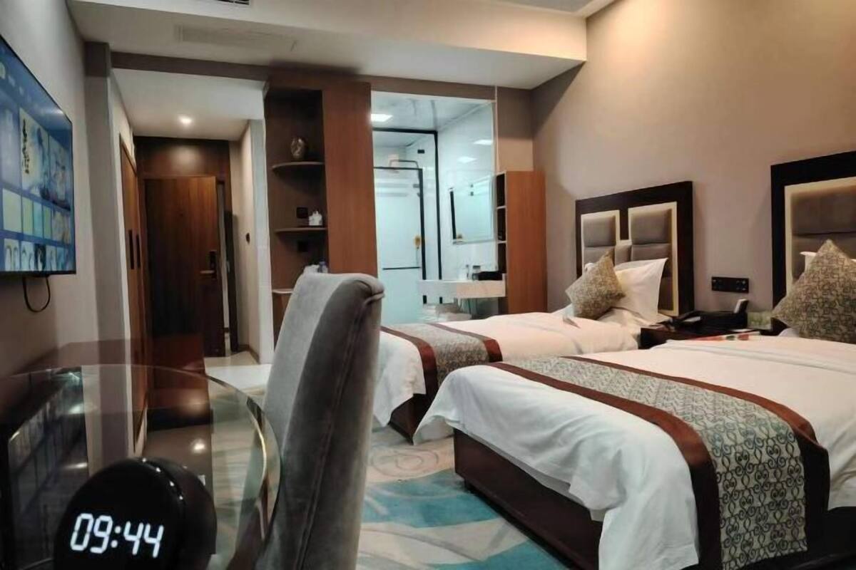 Quarto de hotel com duas camas, uma secretária com relógio e um espelho.