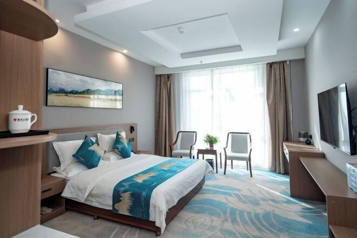 Quarto de hotel com cama, escrivaninha, cadeira, televisão e janela com cortinas.