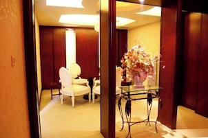 Quarto de hotel com área de estar, mesa de vidro com um vaso de flores e painéis de madeira.