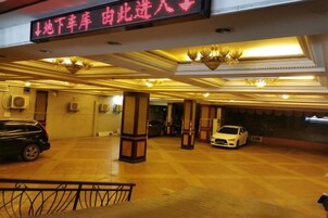 Um amplo estacionamento interno com vários carros estacionados, um painel digital acima e um lustre no teto.