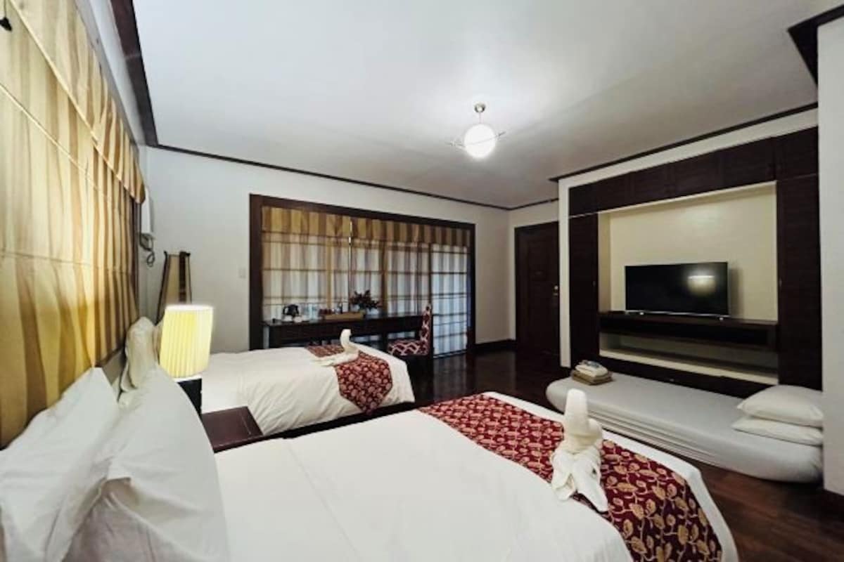 Quarto de hotel com duas camas, televisão, escrivaninha e uma janela grande.