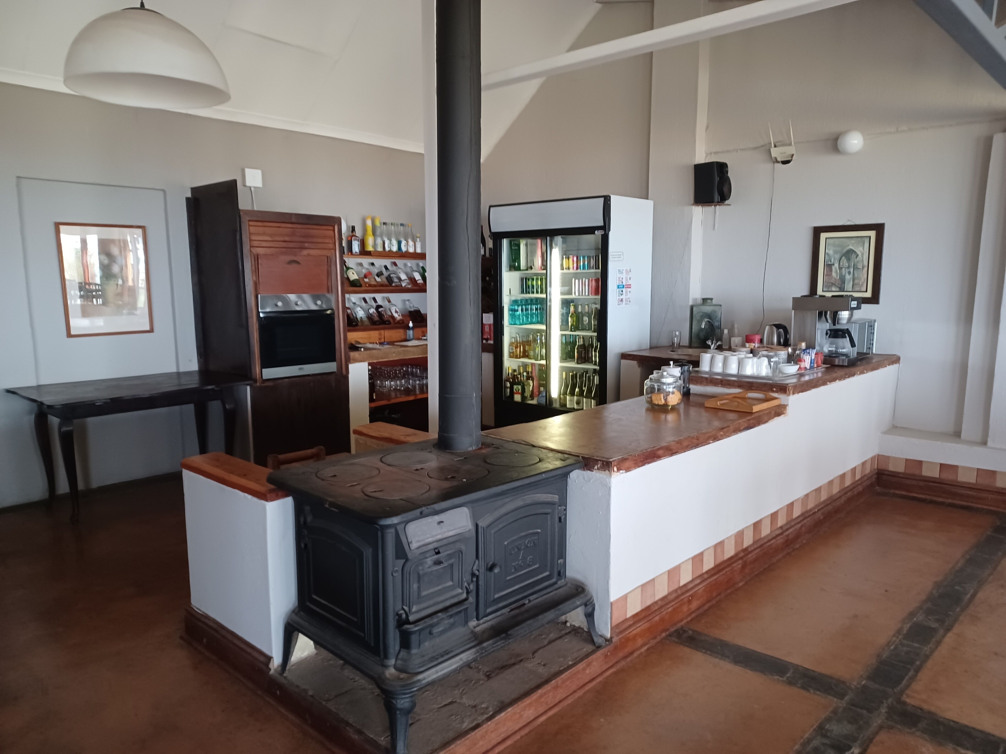 Cozinha com fogão central, geladeira e prateleiras repletas de garrafas e copos.
