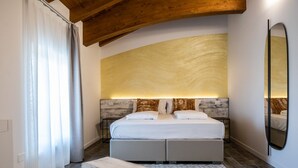 Quarto com cama, mesas de cabeceira, um banquinho, um espelho grande e um tapete estampado.