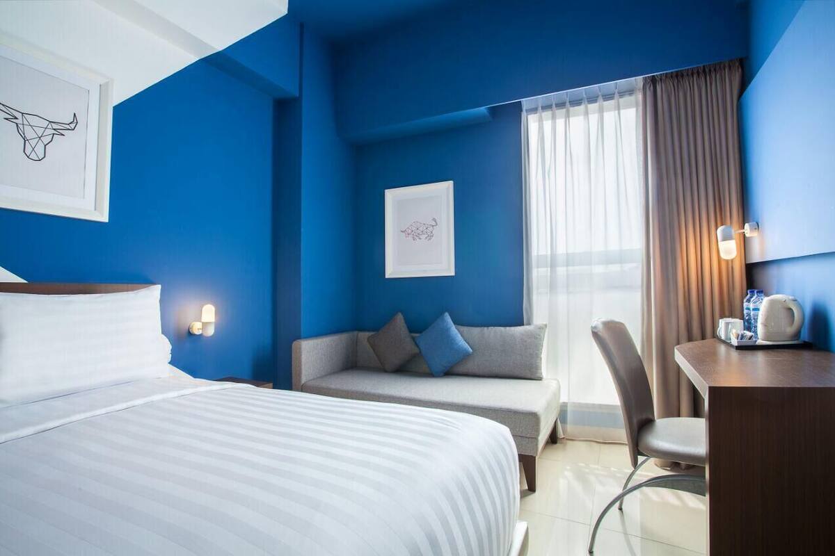 Quarto de hotel com cama, sofá, escrivaninha e cadeira.