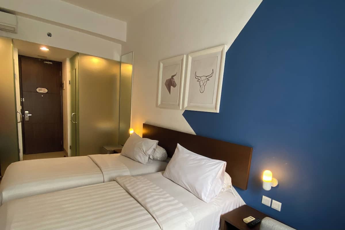 Quarto de hotel com cama, mesa de cabeceira, espelho e duas luminárias na parede.