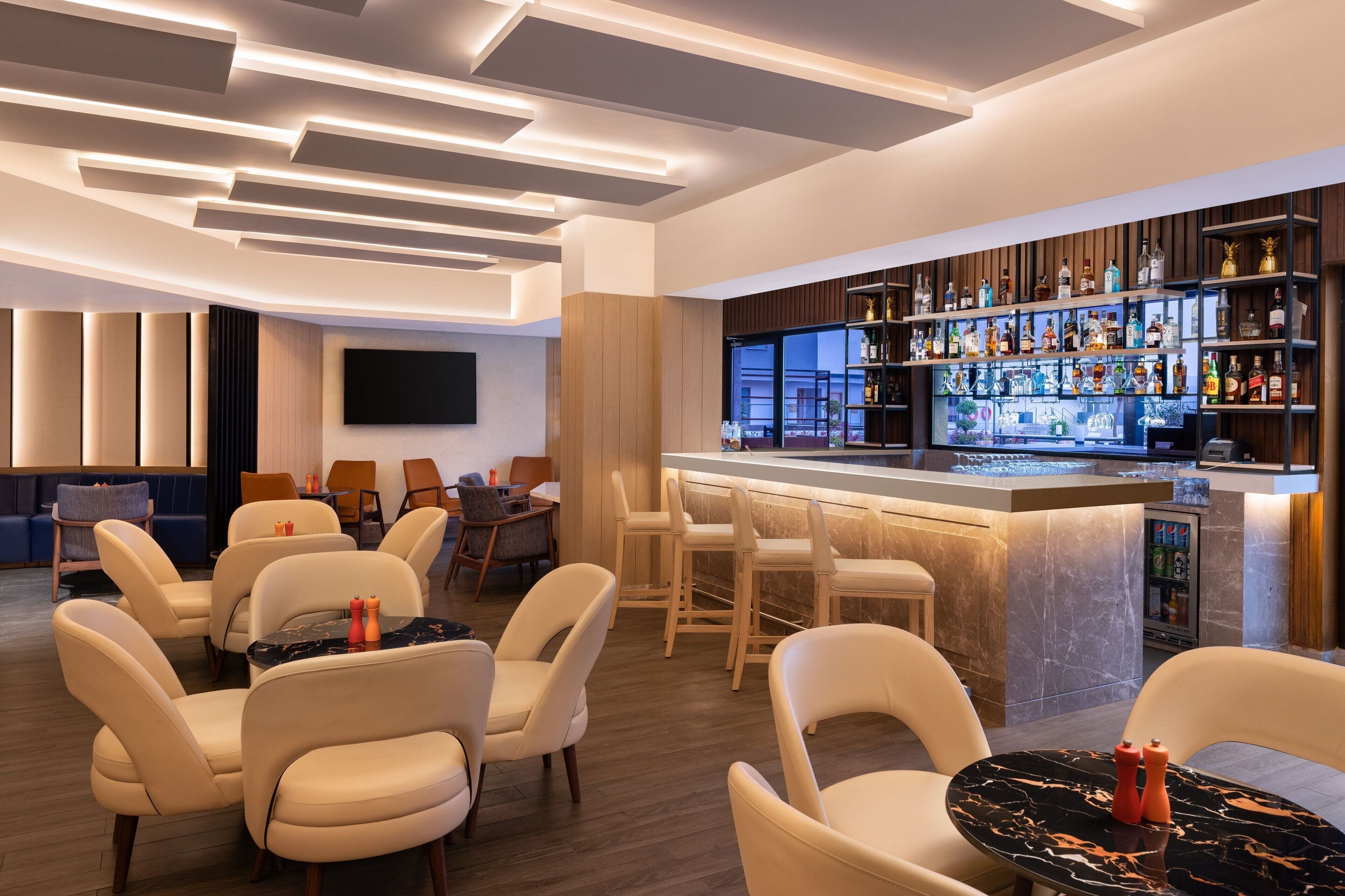 Uma área de bar moderna com um balcão comprido, assentos e uma televisão na parede.