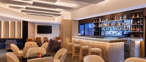 Uma área de bar moderna com um balcão comprido, assentos e uma televisão na parede.