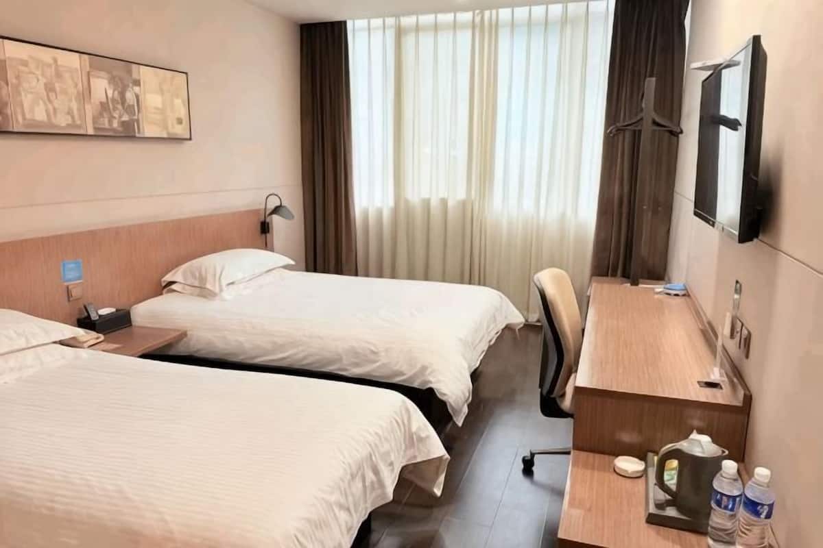 Quarto de hotel com duas camas, uma escrivaninha, uma cadeira, uma televisão e uma janela com cortinas.