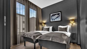 Quarto de hotel moderno com duas camas, uma janela grande com cortinas, um quadro com a placa de Las Vegas e duas luminárias fixadas na parede.