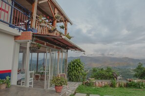 Um edifício de dois andares com varanda, plantas em vasos e vista para montanhas.
