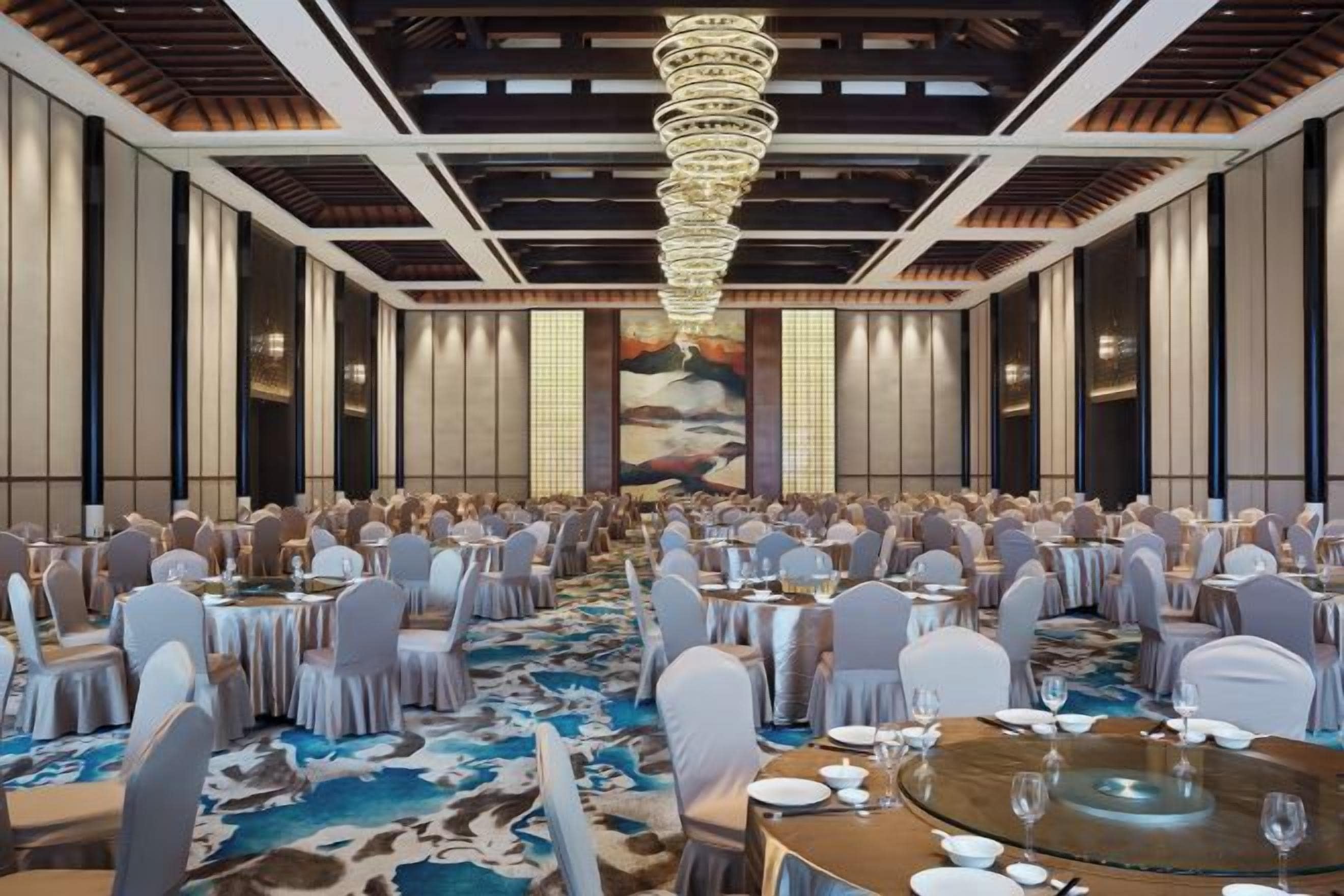 Uma sala de banquetes com mesas redondas, cadeiras e um candelabro.
