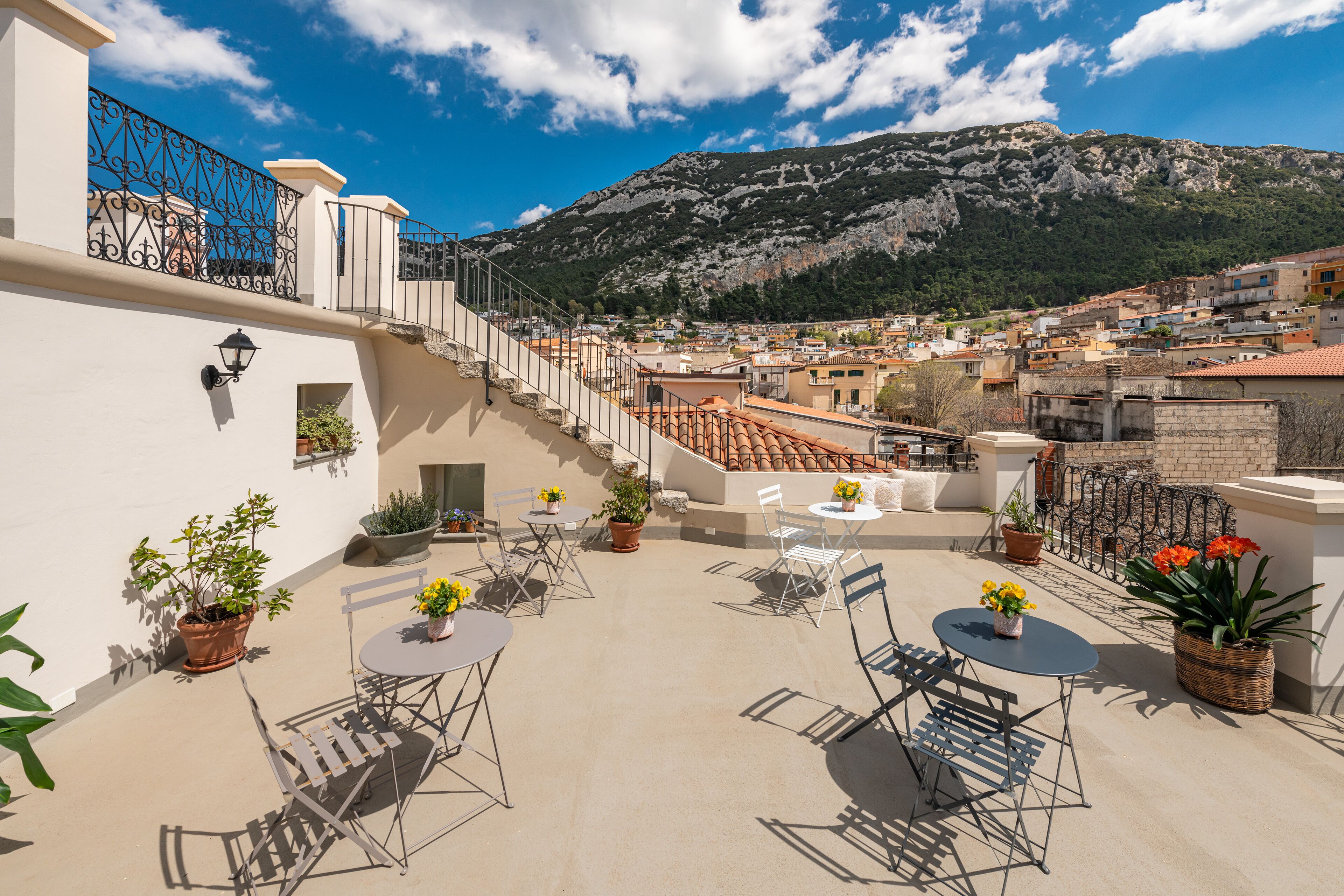Terraço no telhado com área de estar ao ar livre, plantas em vasos e vista para uma cidade montanhosa.