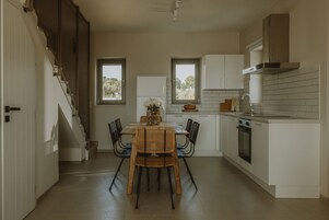 Cozinha moderna com armários brancos, área de jantar com cadeiras de vime e uma escada à esquerda.