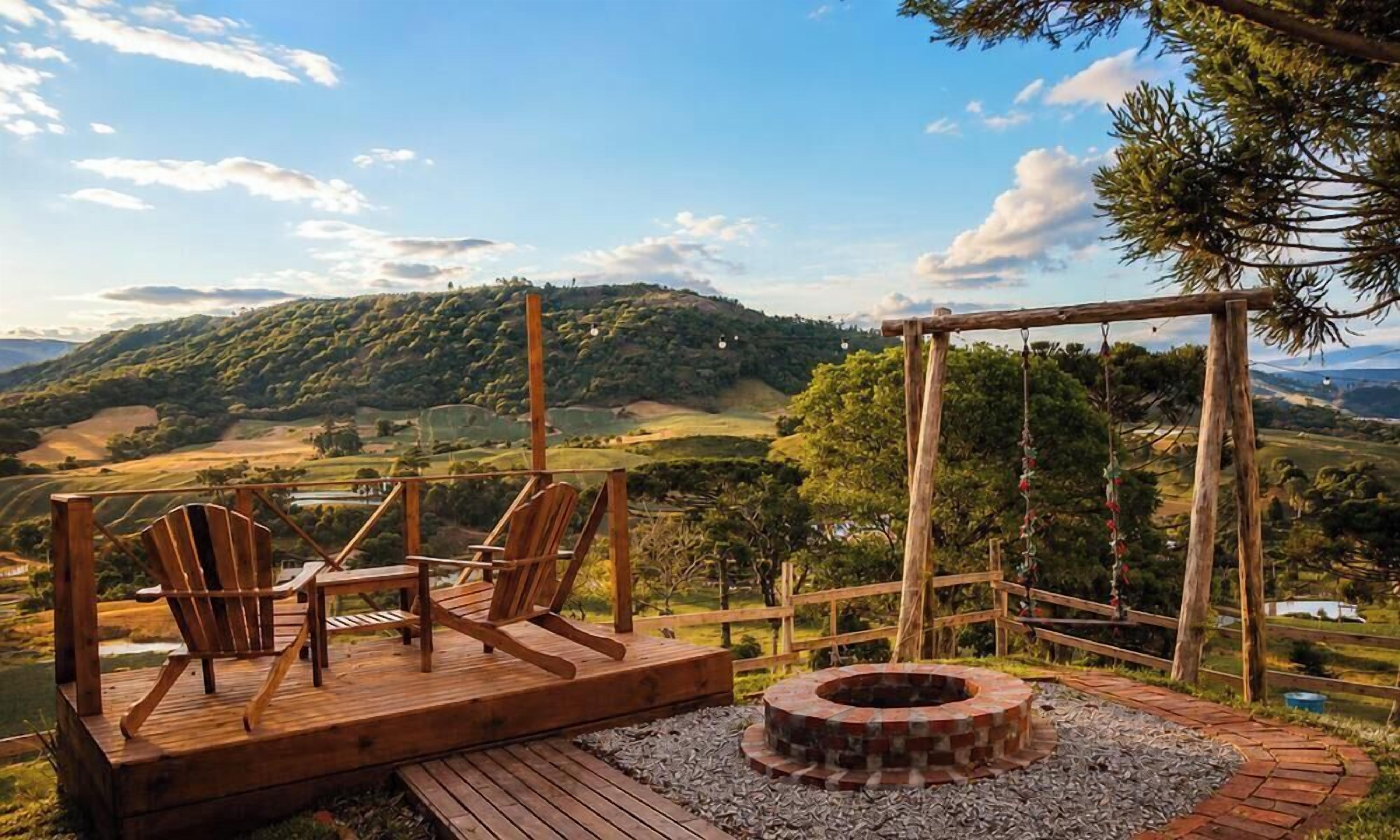 Um deck de madeira com cadeiras e uma lareira, com vista para uma paisagem ondulada.