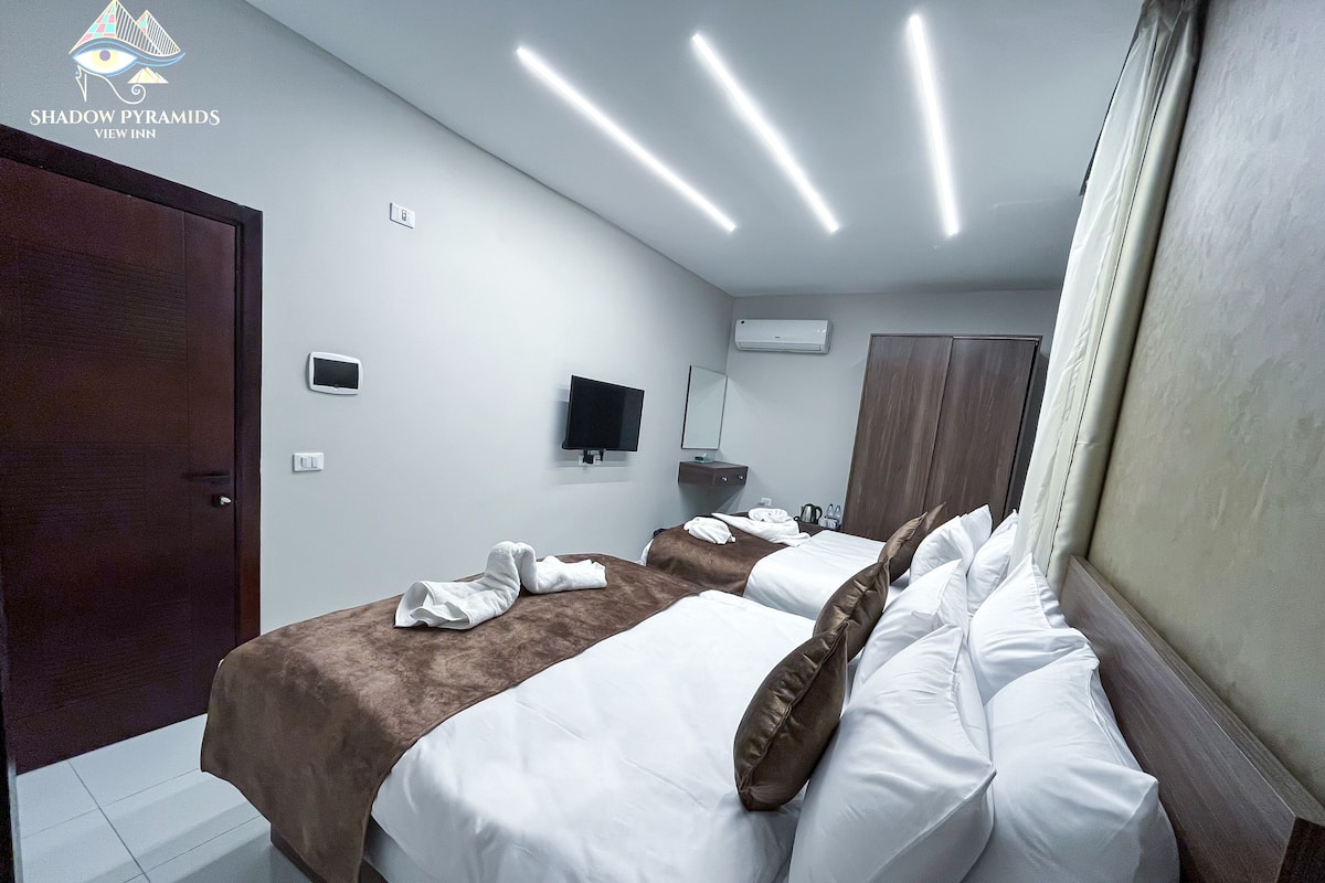 Quarto de hotel com duas camas, televisão, espelho e guarda-roupa.