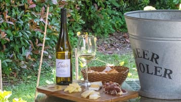 Uma garrafa de vinho, uma taça, queijo e um balde com a inscrição 'BEER' sobre uma mesa ao ar livre.