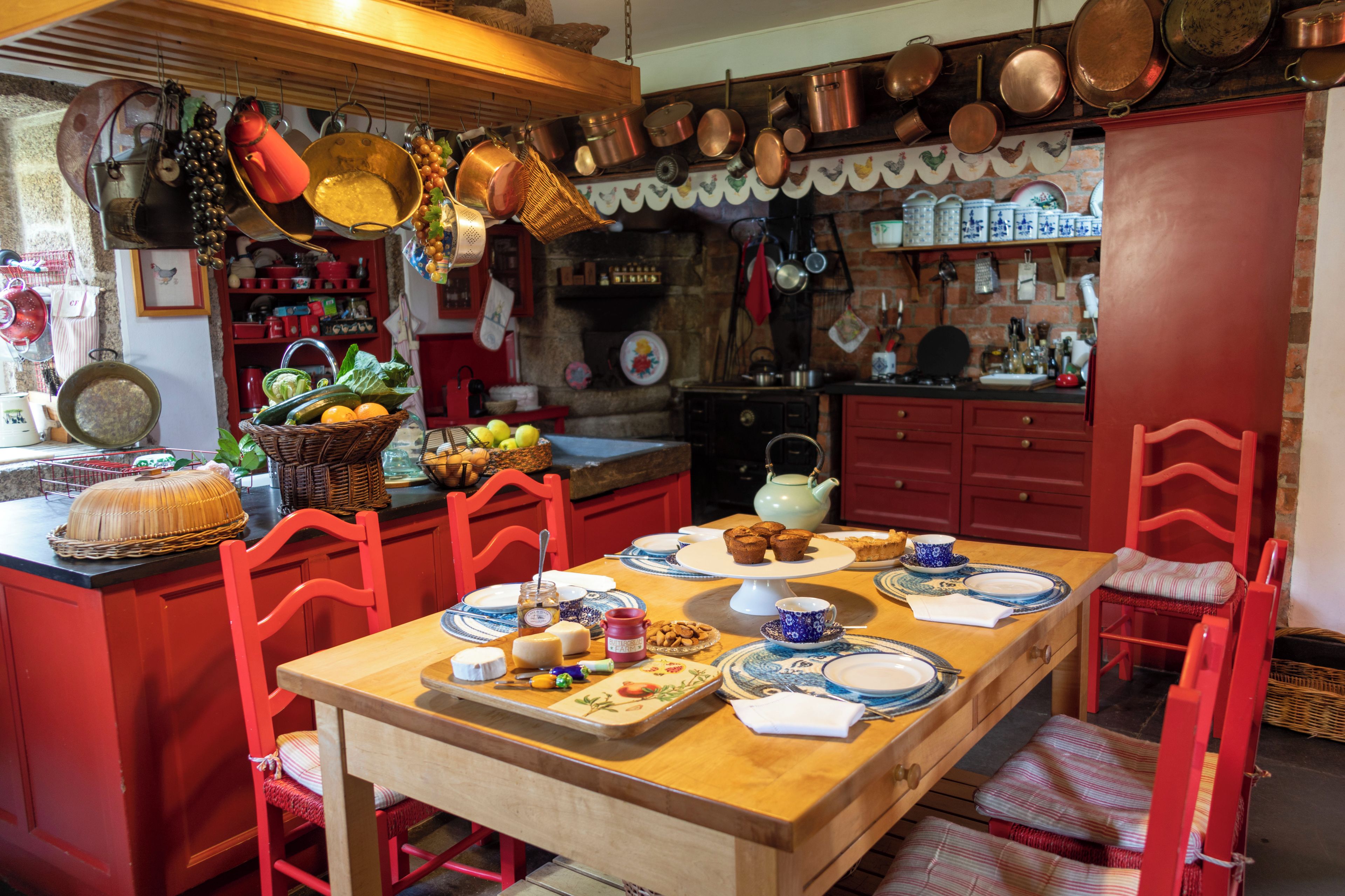 Uma cozinha tradicional com armários de madeira, uma mesa de jantar posta para quatro pessoas e diversos utensílios e eletrodomésticos.