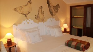 Quarto com cama, duas luminárias de cabeceira e um mural de galinhas na parede.