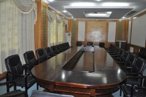 Uma sala de conferências com uma mesa comprida e cadeiras, uma tela de projetor e um quadro branco.