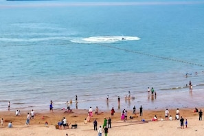 Uma praia com pessoas, uma barreira de corda e águas calmas.