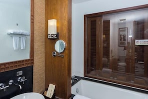 Uma casa de banho com porta de madeira, espelho, porta-toalhas, lavatório e janela com persianas.