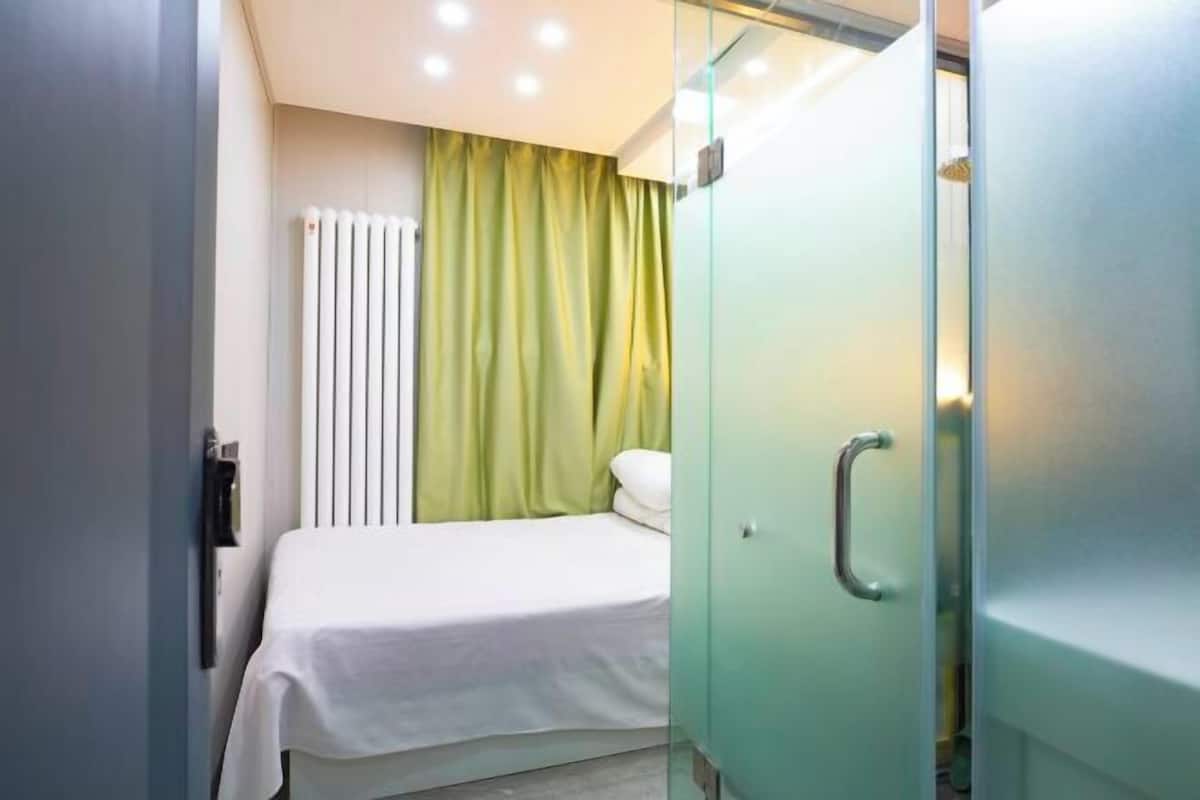 Quarto pequeno e moderno com cama, radiador e cortina verde.