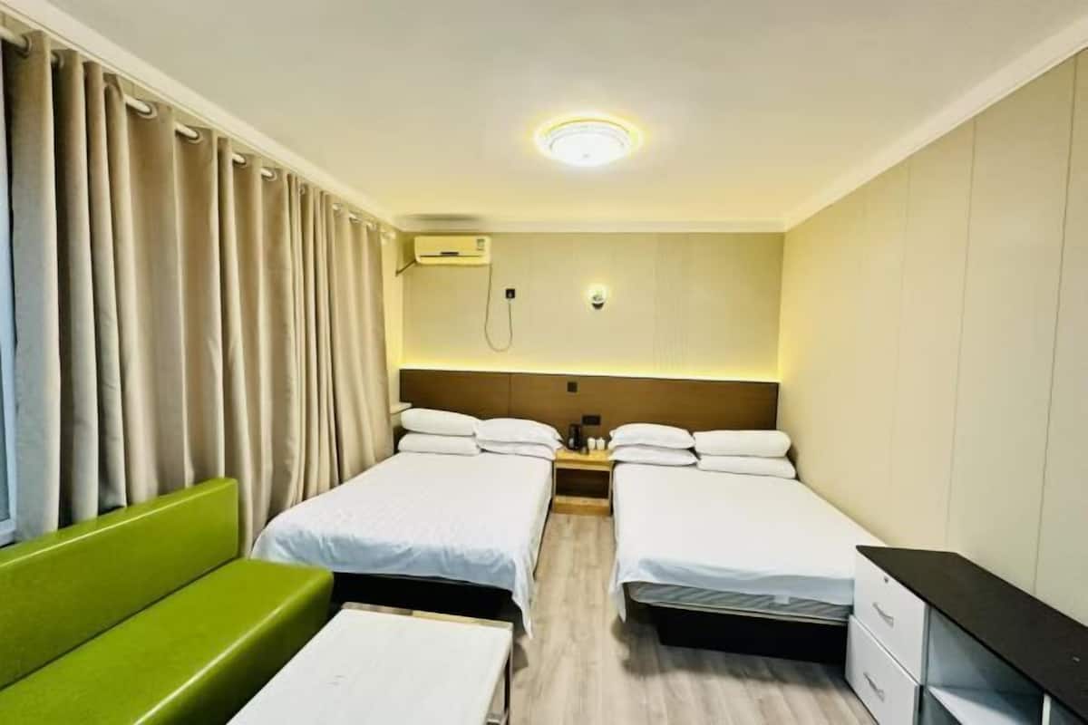 Quarto de hotel com duas camas, um sofá verde, uma mesinha e uma escrivaninha com gavetas.