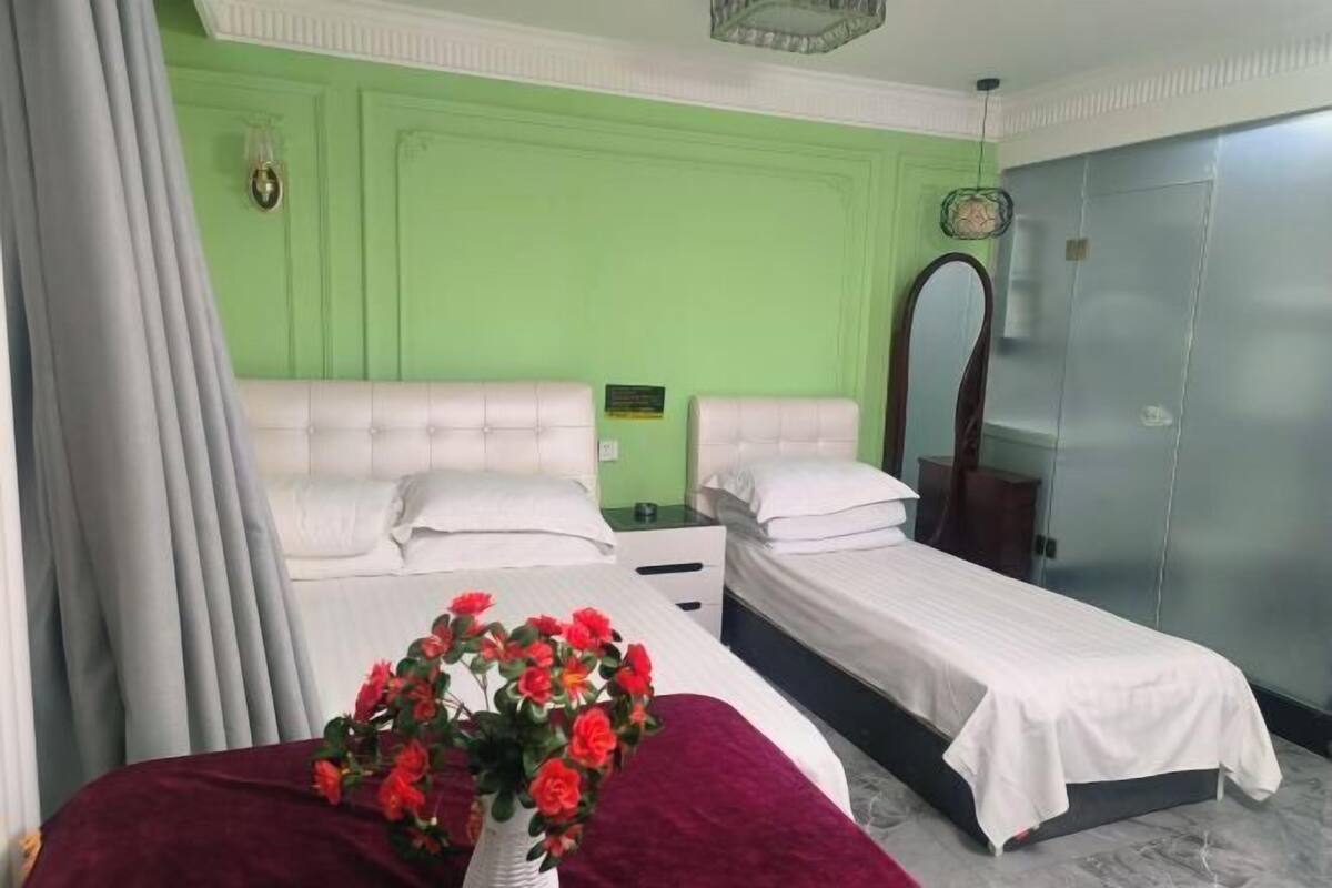Quarto de hotel com duas camas, um espelho, um guarda-roupa e um vaso com flores.
