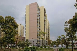 Edifício residencial de vários andares com varandas, cercado por vegetação e carros estacionados.