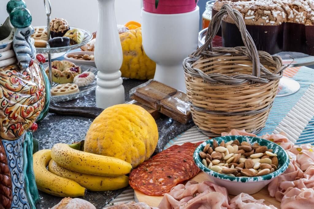 Diversos alimentos, incluindo bananas, uma abóbora amarela grande, salame fatiado, amêndoas e doces sobre uma mesa.