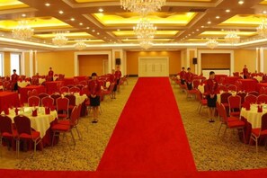 Uma sala de banquetes com mesas redondas, tapete vermelho e lustres.